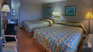 Quarto de hotel com duas camas, uma escrivaninha, uma cadeira e um abajur.