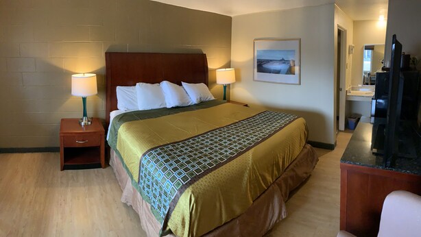 Quarto de hotel com cama, duas luminárias de cabeceira, um quadro na parede e uma TV.