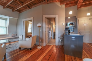Um interior moderno com teto de madeira, cozinha com micro-ondas, área de bar e espaço de estar com sofá e luminária de chão.