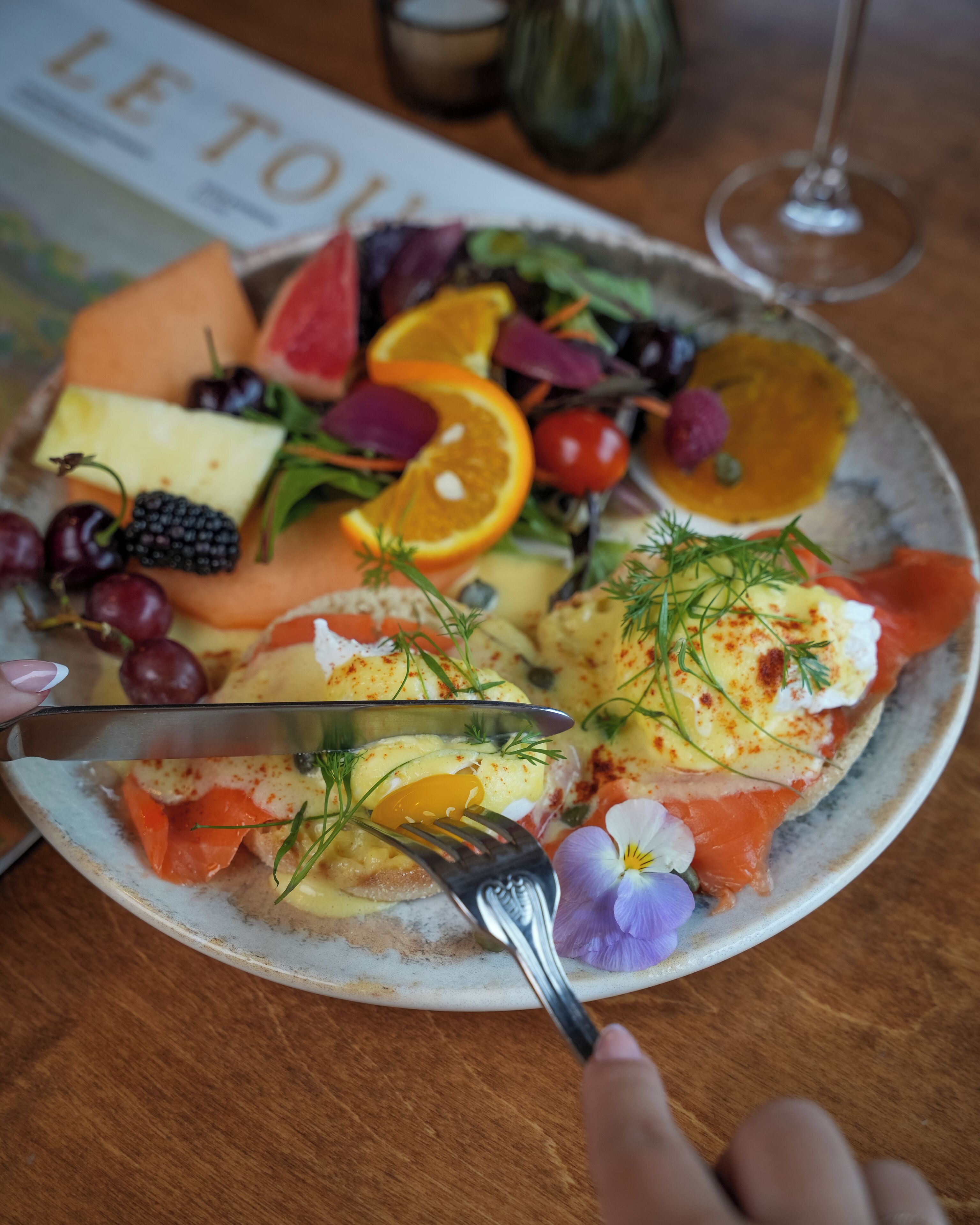 Um prato de comida com várias frutas e uma taça de vinho sobre uma mesa.
