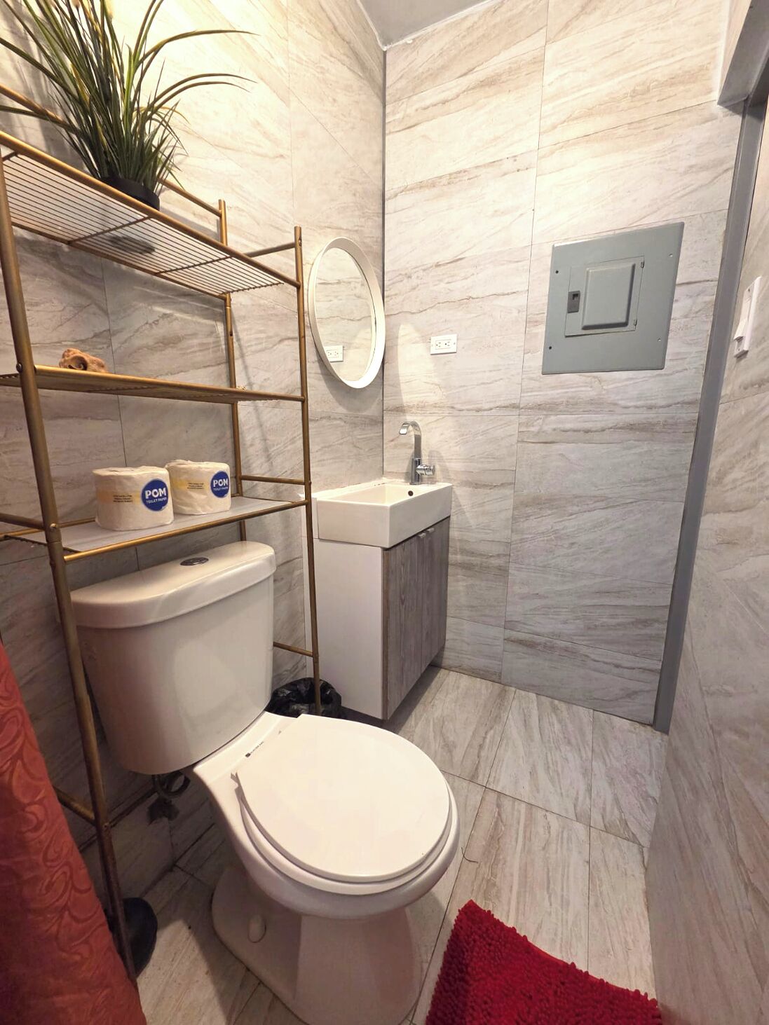 Casa de banho compacta com sanita, lavatório e prateleira com artigos de higiene pessoal.