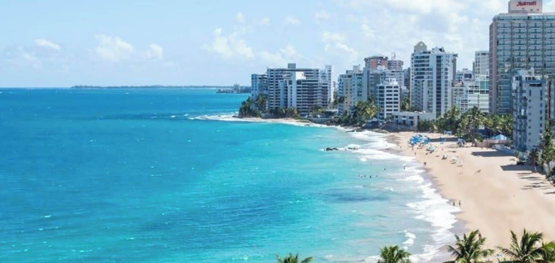 Paisagem costeira com praia, hotéis altos e águas azul-claras.