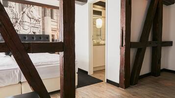 Quarto com cama, vigas de madeira e banheiro visível através de uma porta aberta.