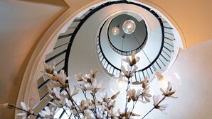 Escadaria em espiral com corrimão branco e uma árvore com flores brancas na base.