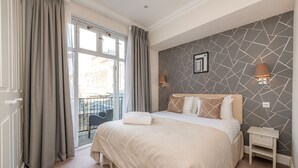 Quarto de hotel com uma cama grande, uma varanda com uma cadeira e uma parede com padrão geométrico.