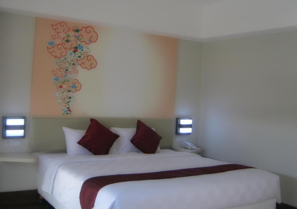 Quarto de hotel com uma cama, duas almofadas, mesa de cabeceira com telefone e uma decoração na parede.