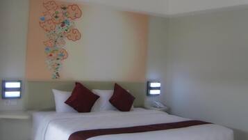 Quarto de hotel com uma cama, duas almofadas, mesa de cabeceira com telefone e uma decoração na parede.