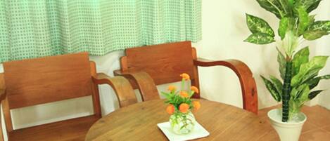 Uma sala de jantar com uma mesa redonda de madeira, duas cadeiras, um vaso com flores e uma planta em vaso.