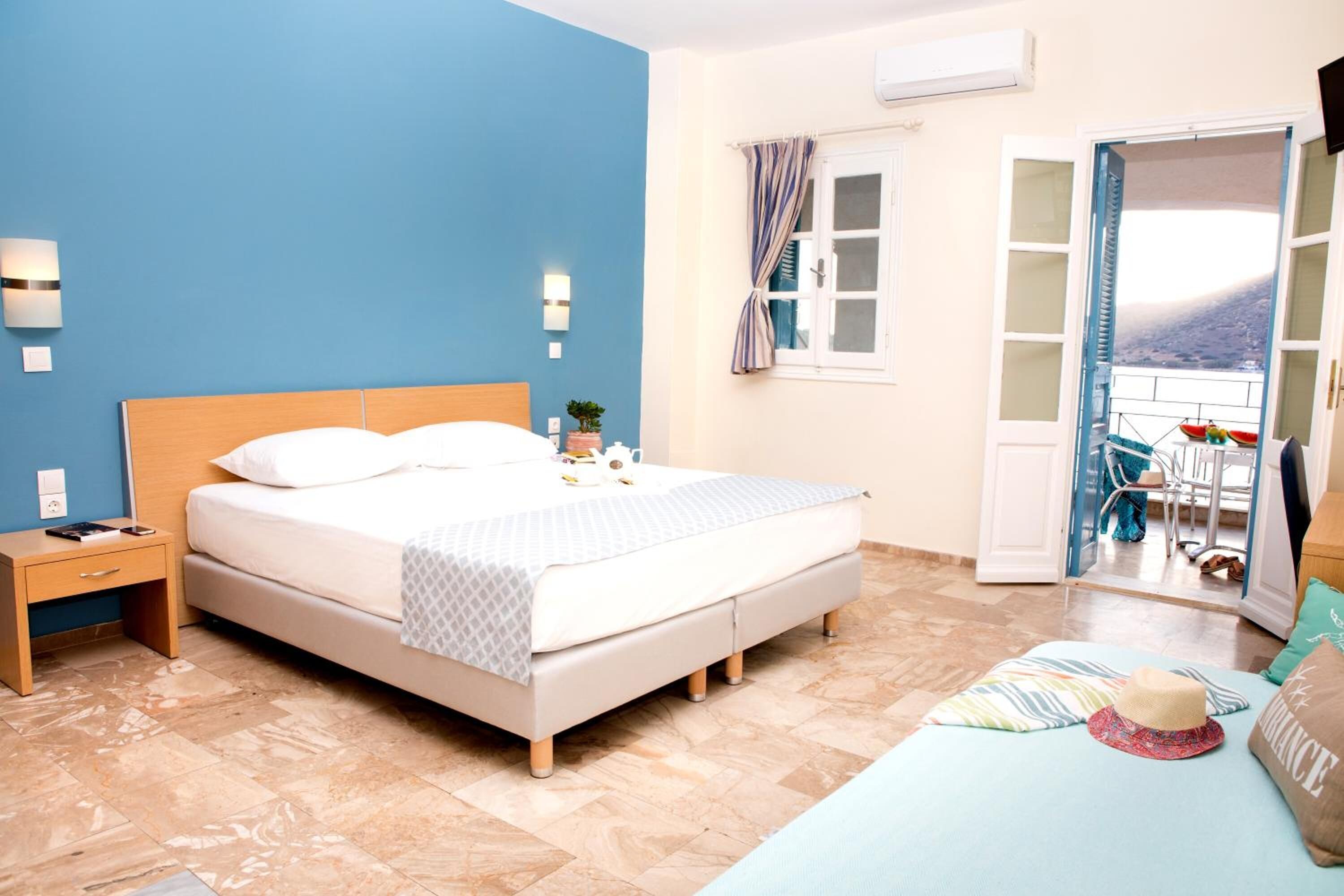 Quarto com cama, mesa de cabeceira e vista para a varanda.