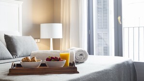 Cama arrumada com uma bandeja de itens de café da manhã, incluindo croissants, morangos e suco de laranja, em um quarto de hotel com vista para a cidade.