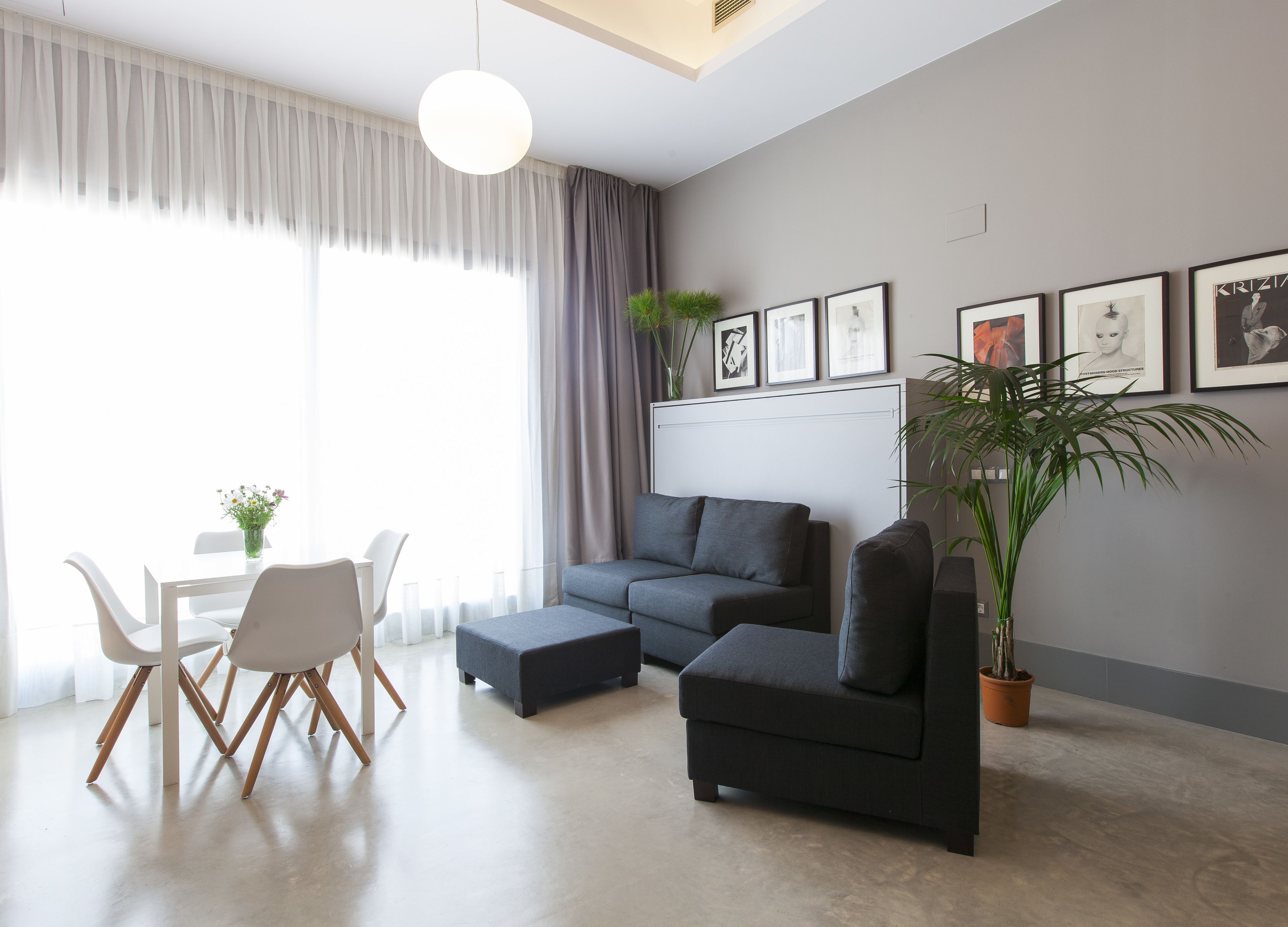 Uma sala moderna com um sofá cinzento, uma mesa de centro e um espaço de jantar com mesa e cadeiras brancas.
