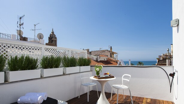 Terraço no telhado com deck de madeira, mobiliário de exterior branco e vista para a cidade e o mar.