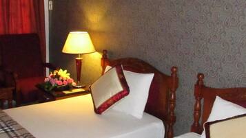 Quarto de hotel com duas camas, uma mesa de cabeceira com abajur e um arranjo floral.