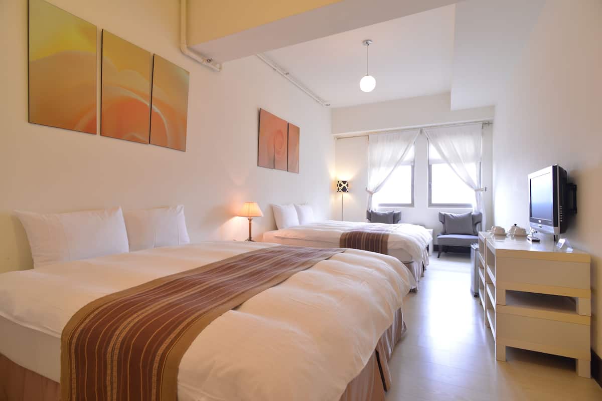 Quarto de hotel com duas camas, televisão, escrivaninha e janela com cortinas.