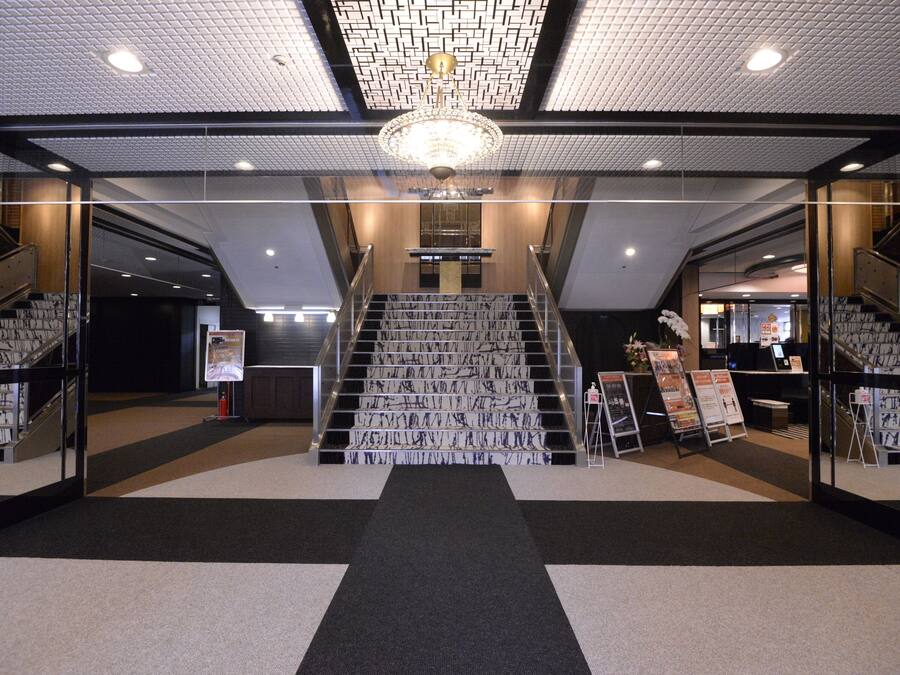 Um hall de hotel moderno com uma escadaria central, paredes de vidro e teto trabalhado.