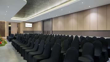 Sala de conferência com fileiras de cadeiras, uma tela grande exibindo um logotipo e um design moderno no teto.