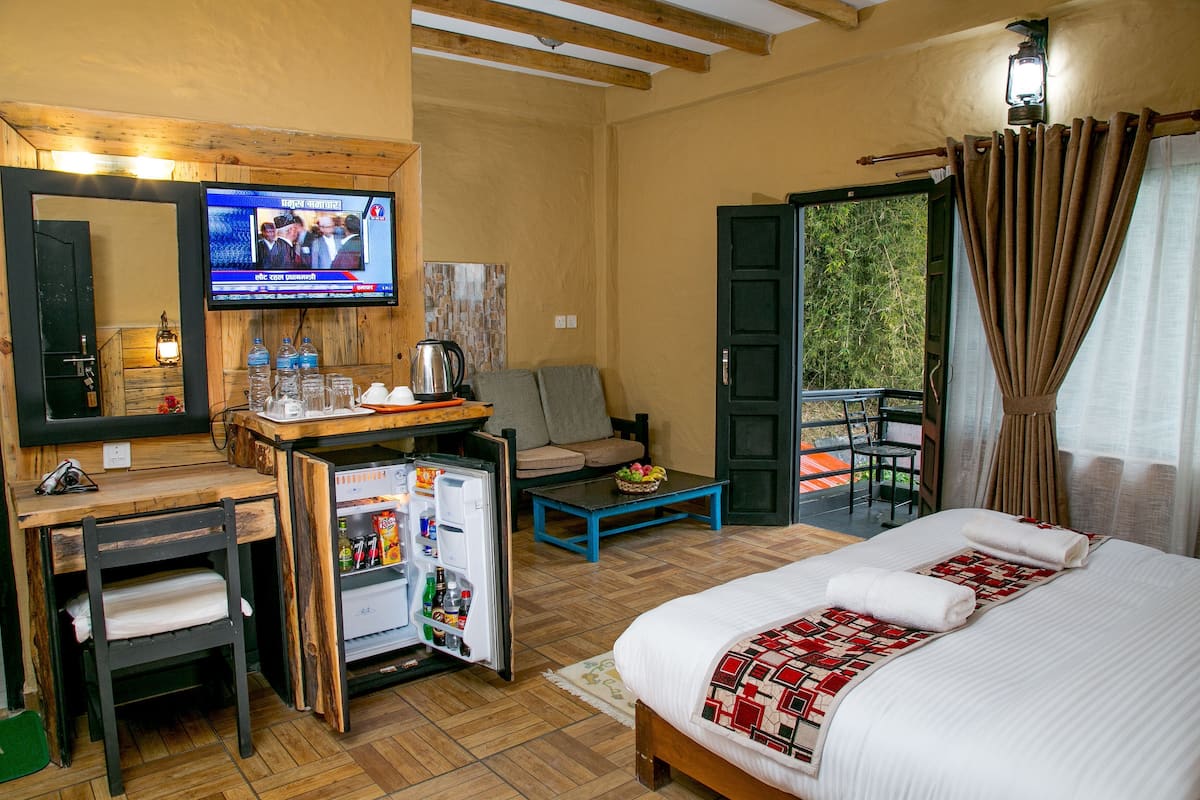 Quarto com cama, escrivaninha com televisão, um frigorífico pequeno e varanda com cadeira.