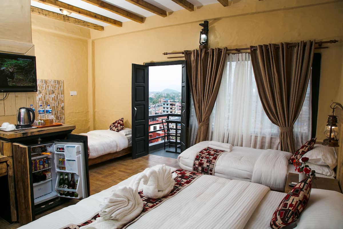 Quarto de hotel com duas camas, uma kitchenette pequena, televisão e varanda com vista para a cidade.
