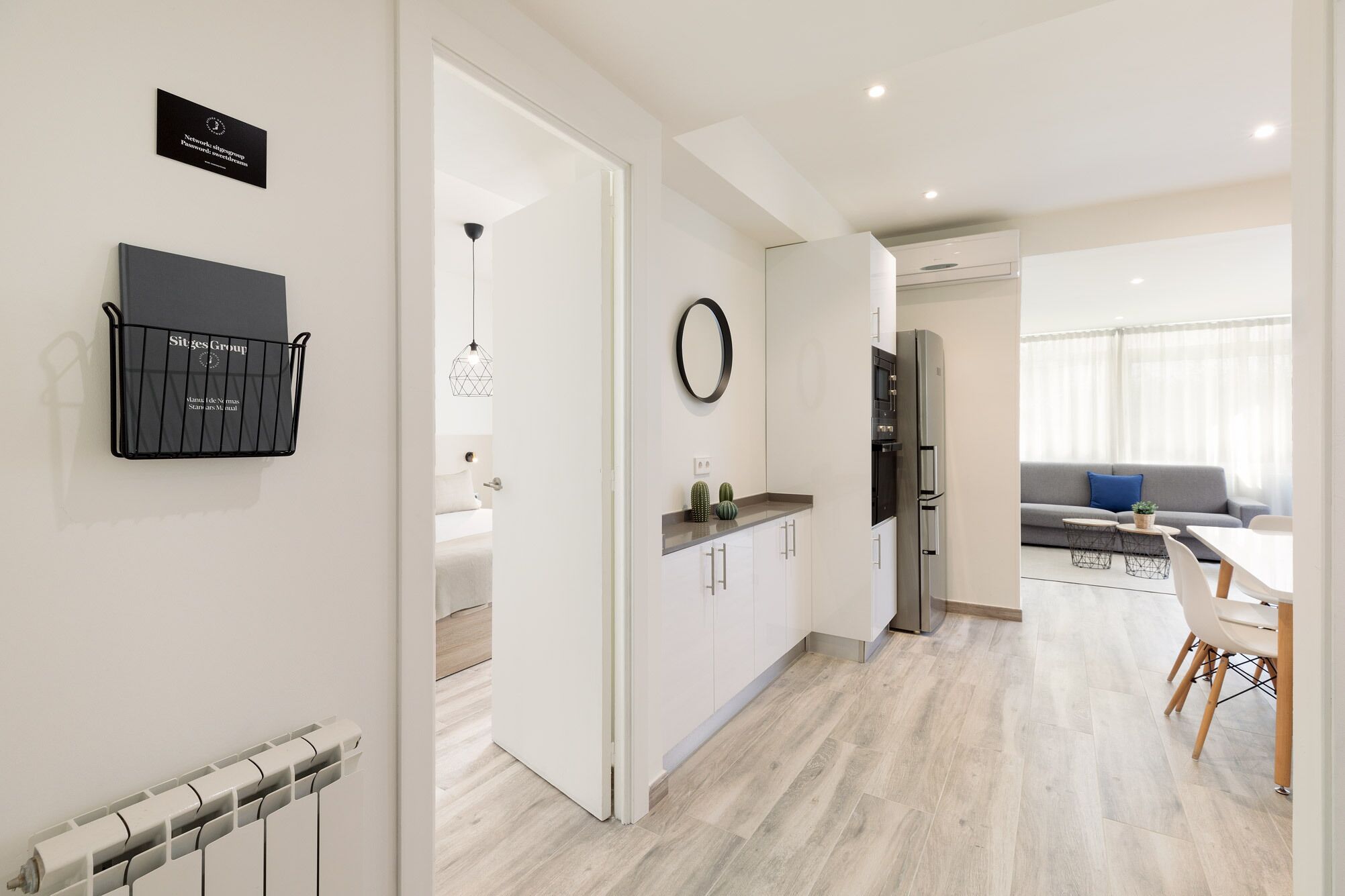 Cozinha moderna com armários brancos, forno embutido e bancada. Há uma área de jantar com mesa e cadeiras, e uma sala de estar com sofá e mesa de centro.