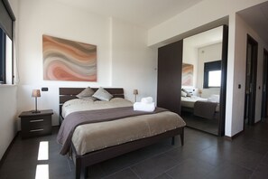 Quarto moderno com uma cama grande, mesas de cabeceira, uma obra de arte na parede e um espelho refletindo o ambiente.