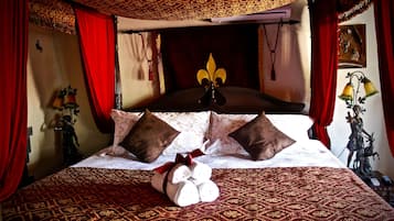Uma cama com um cobreleito estampado, duas almofadas castanhas e uma toalha branca com laço vermelho.