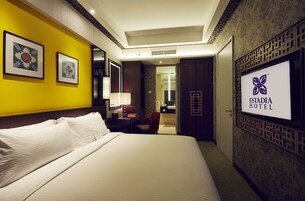 Quarto de hotel com uma cama grande, uma escrivaninha, uma cadeira e um banheiro visível por uma porta aberta.