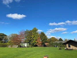 Um campo gramado com uma pequena casa móvel branca, um galpão de madeira e uma estrutura semelhante a uma tenda.