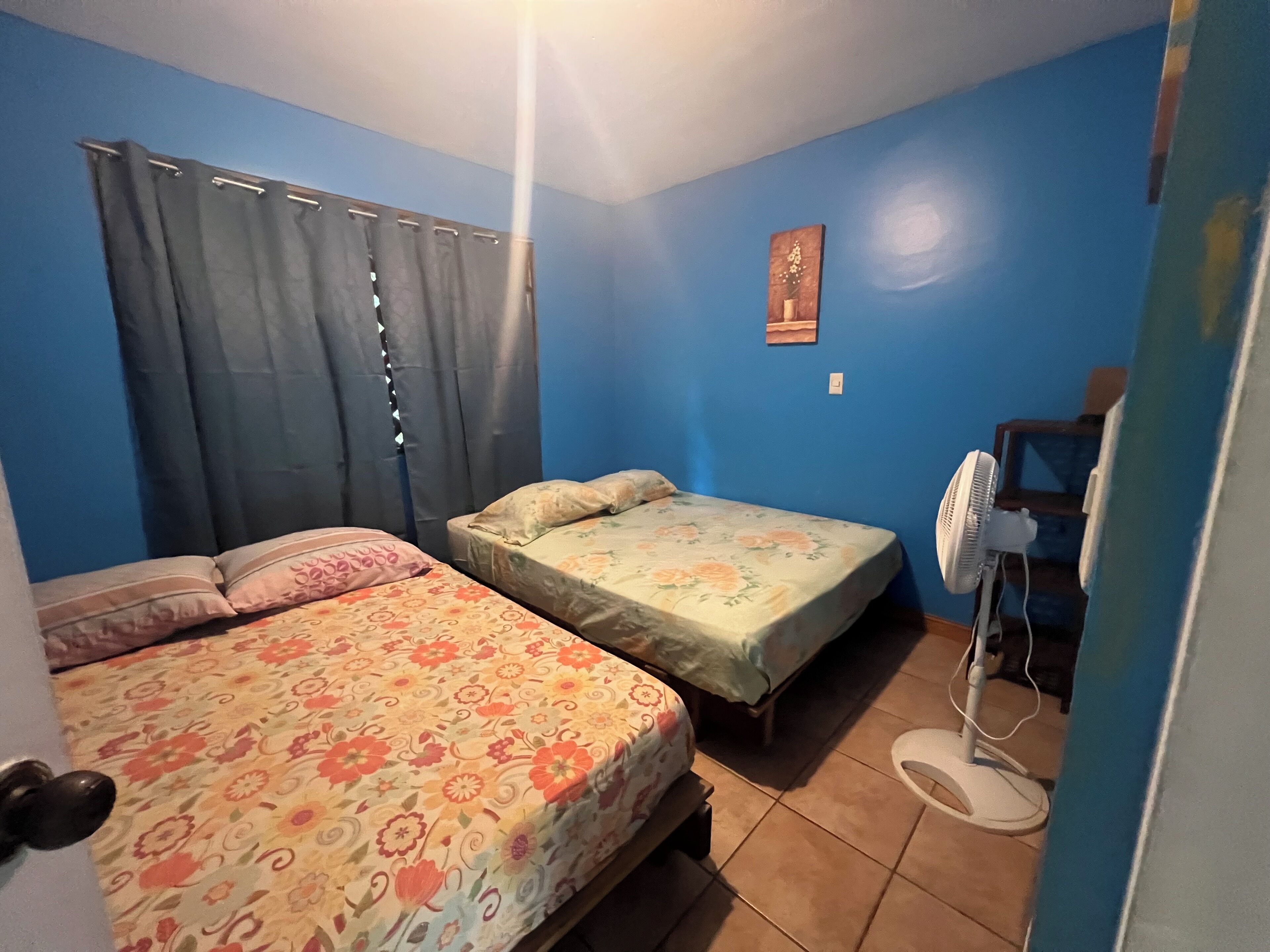Quarto com duas camas, um ventilador de teto e uma janela com cortinas.
