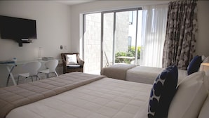 Quarto de hotel com duas camas, uma escrivaninha, uma cadeira, televisão e varanda com cortinas.