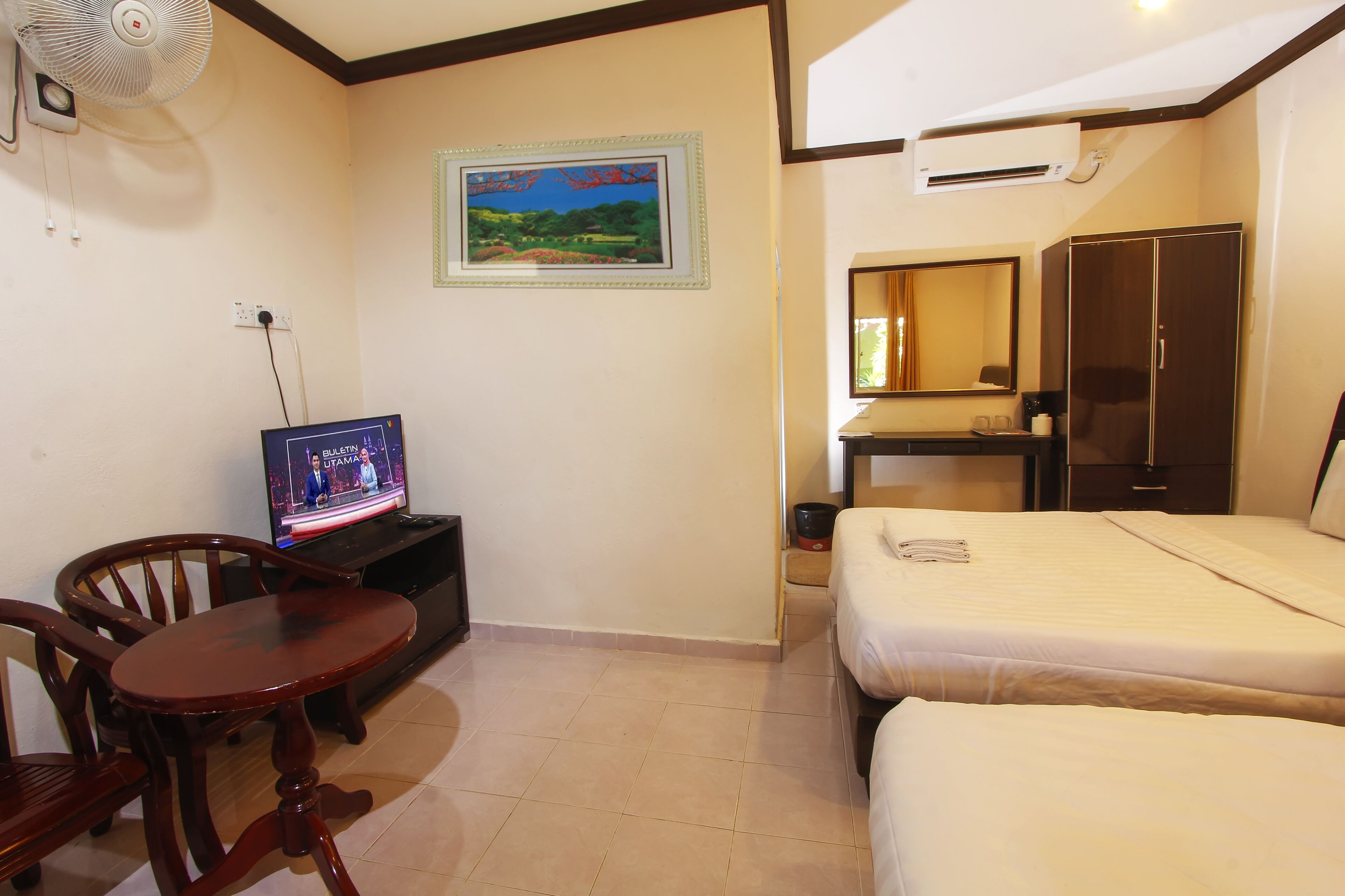Quarto de hotel com duas camas, televisão, escrivaninha, cadeira, guarda-roupa e um quadro na parede.