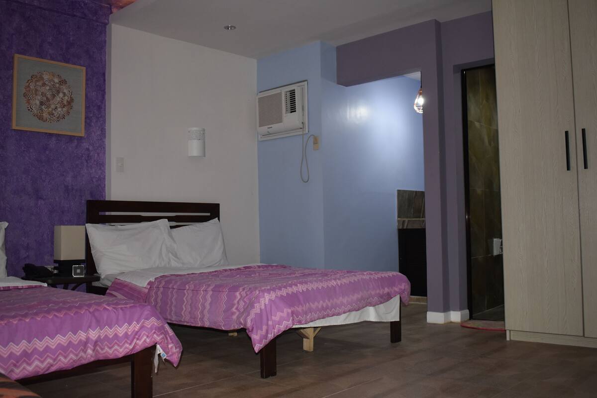 Quarto com duas camas, ar condicionado, mesa de cabeceira com abajur e guarda-roupa.