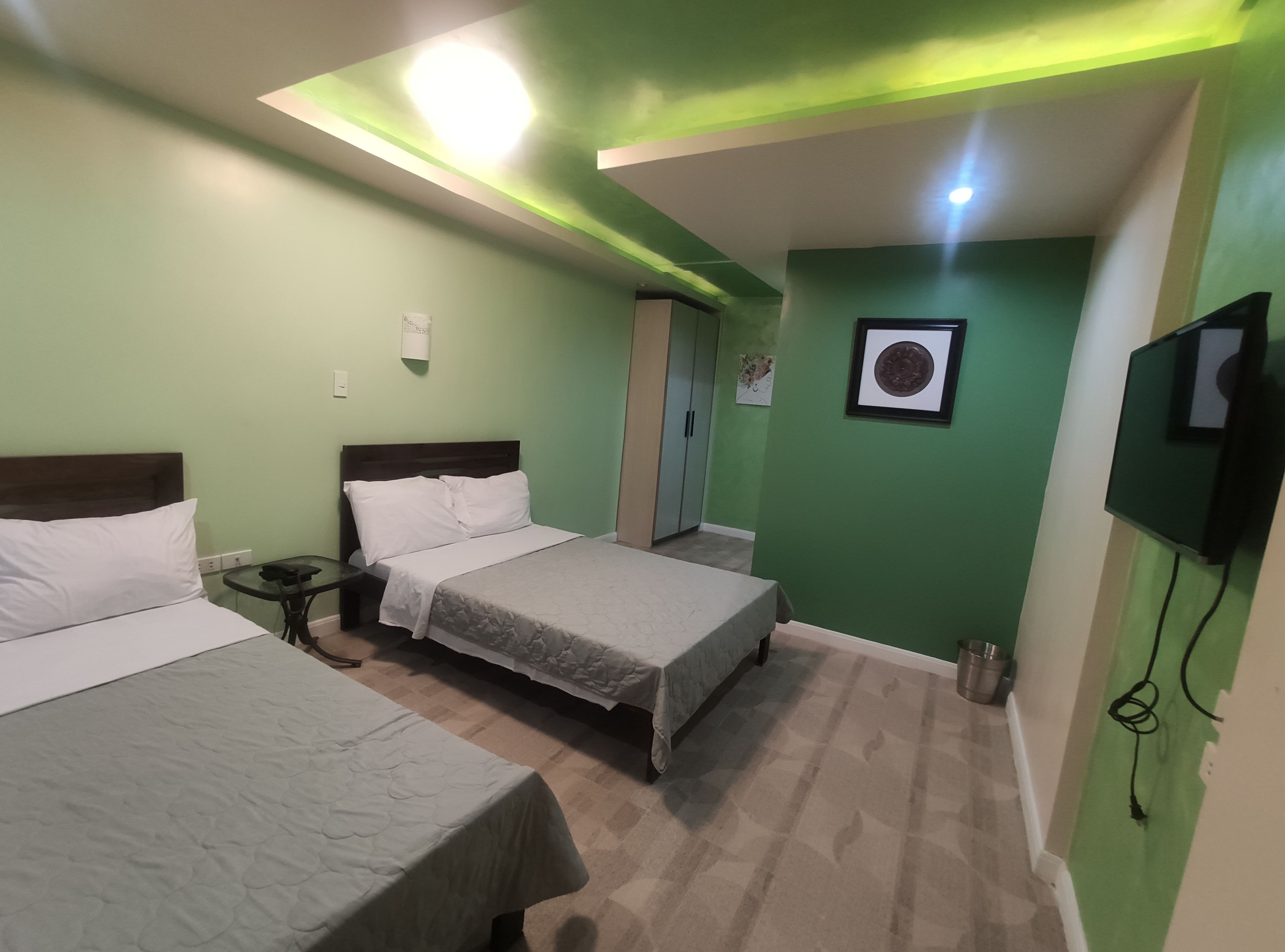Quarto de hotel com duas camas, uma mesinha, televisão e parede verde.