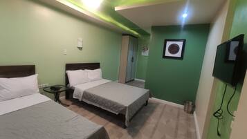Quarto de hotel com duas camas, uma mesinha, televisão e parede verde.
