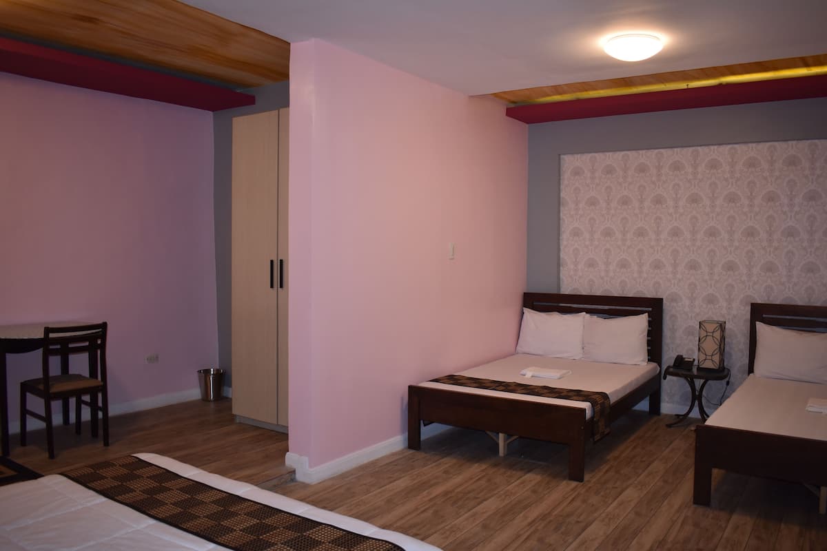 Quarto com duas camas, piso de madeira e uma pequena mesa com abajur.