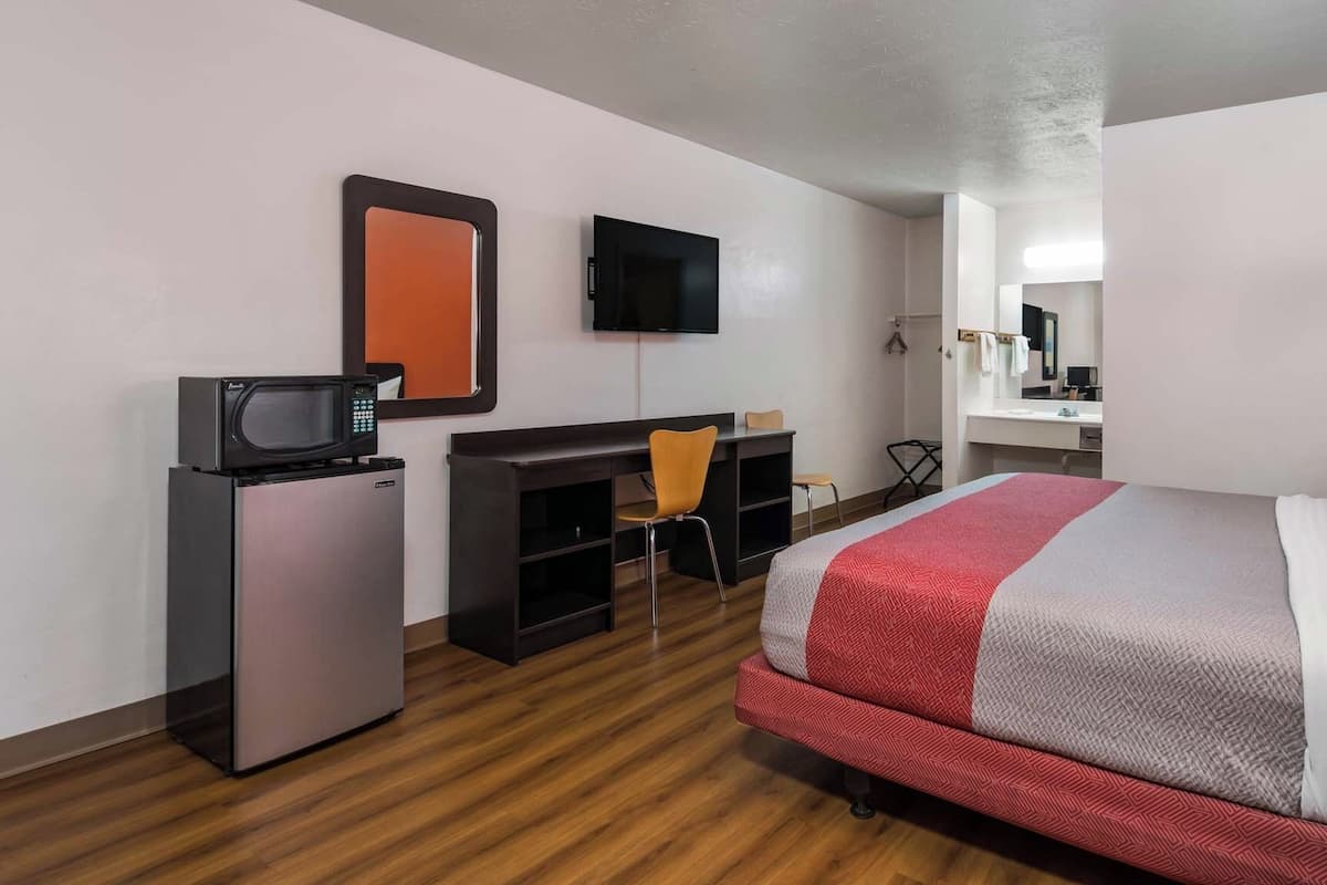 Quarto de hotel com cama, escrivaninha, cadeira, televisão, frigorífico e espelho.