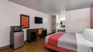 Quarto de hotel com uma cama, uma escrivaninha com cadeira, micro-ondas e televisão.