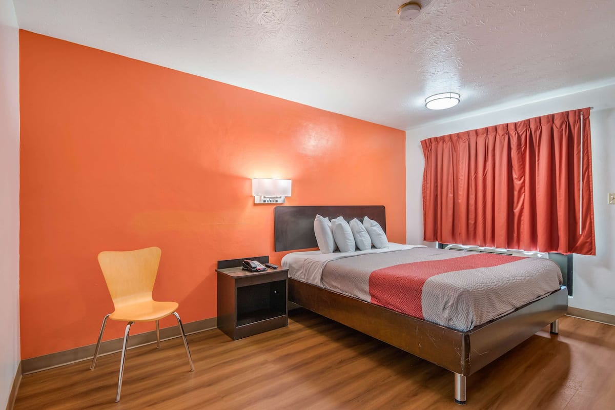 Quarto de hotel com cama, mesa de cabeceira, uma cadeira e parede com esquema de cores vermelho.