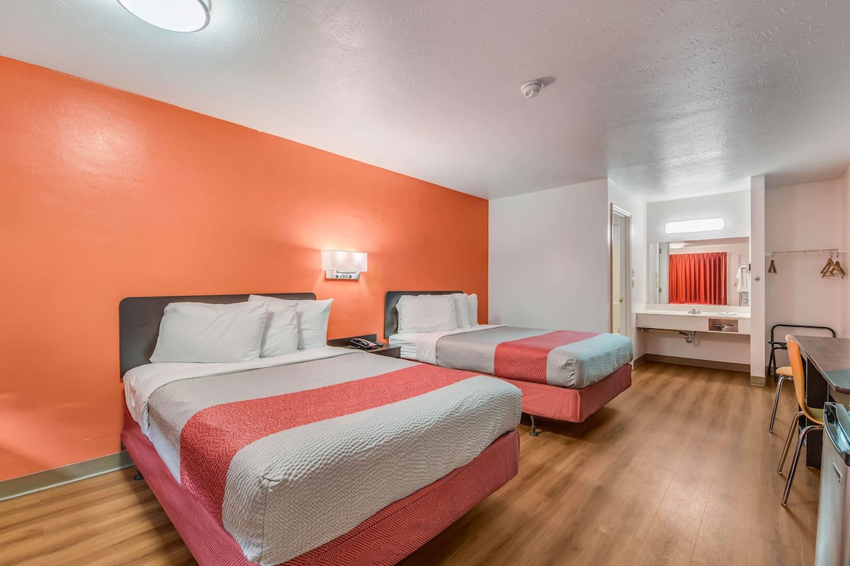 Quarto de hotel com duas camas, uma escrivaninha e um espelho.