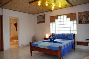 Quarto com cama de madeira, janela com vista, vaso e quadro na parede.