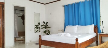 Um quarto com cama de madeira, roupa de cama branca, cortina azul e um espelho na parede.