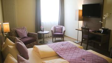 Quarto de hotel com uma cama, duas poltronas, uma mesa de trabalho, uma televisão e um candeeiro.