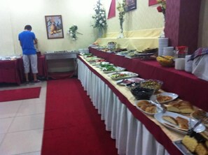 Uma mesa de buffet com diversos alimentos e uma pessoa ao lado do balcão.