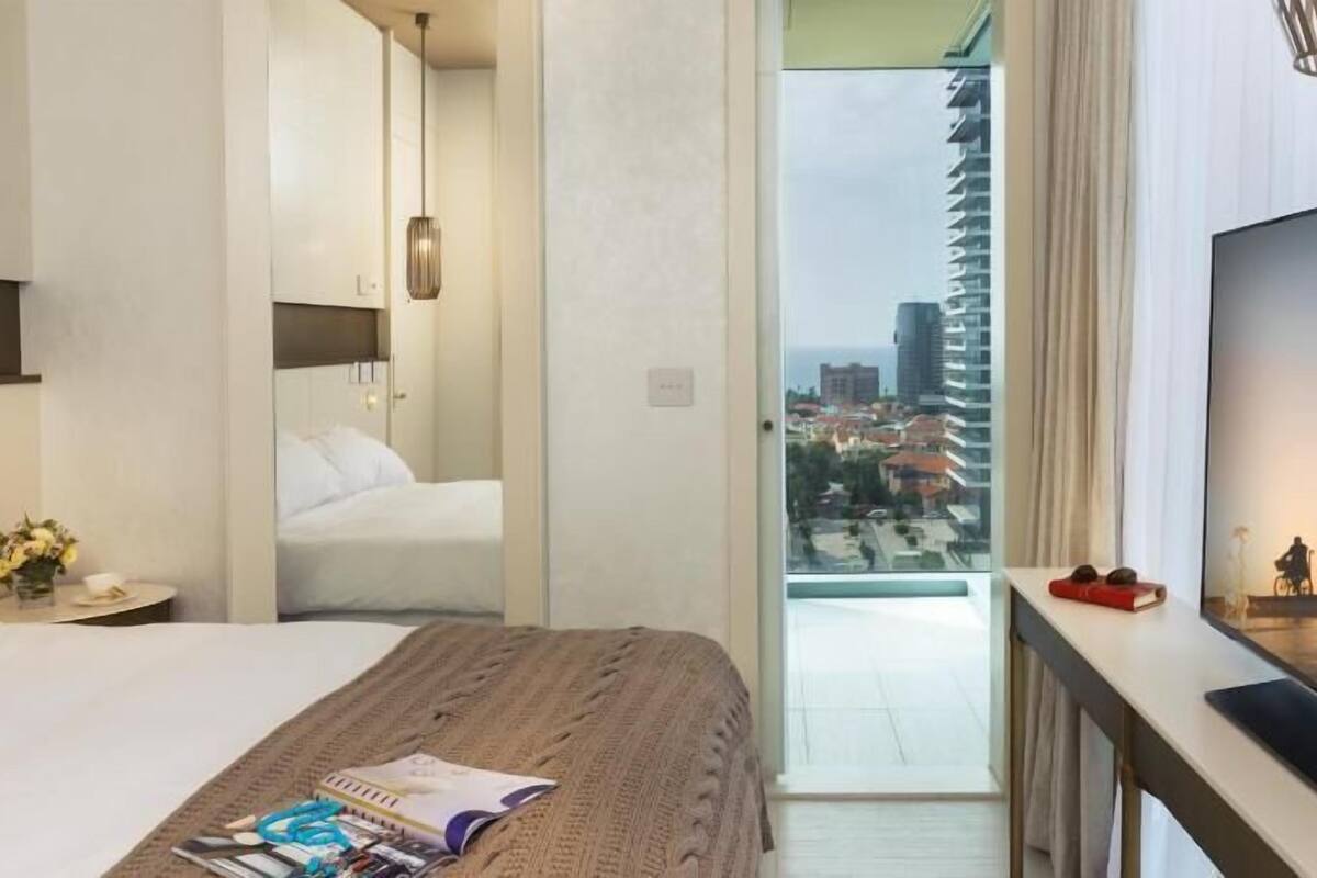 Quarto de hotel com cama, televisão, varanda com vista para a cidade e porta que dá para outro quarto.
