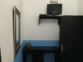 Quarto com espelho, televisão sobre suporte, mesa pequena com cesta e porta.