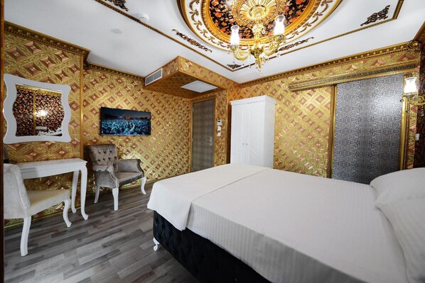 Quarto de hotel com uma cama grande, uma escrivaninha, uma cadeira e uma televisão.