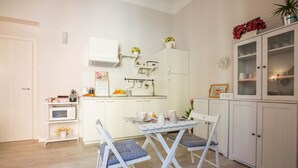 Uma cozinha compacta com armários brancos, uma mesa de jantar com cadeiras e uma pequena geladeira.