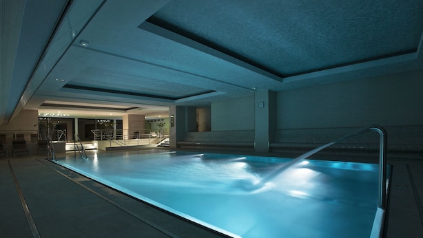 Piscina interior com pistas demarcadas, bloco de partida e cadeira do salva-vidas.
