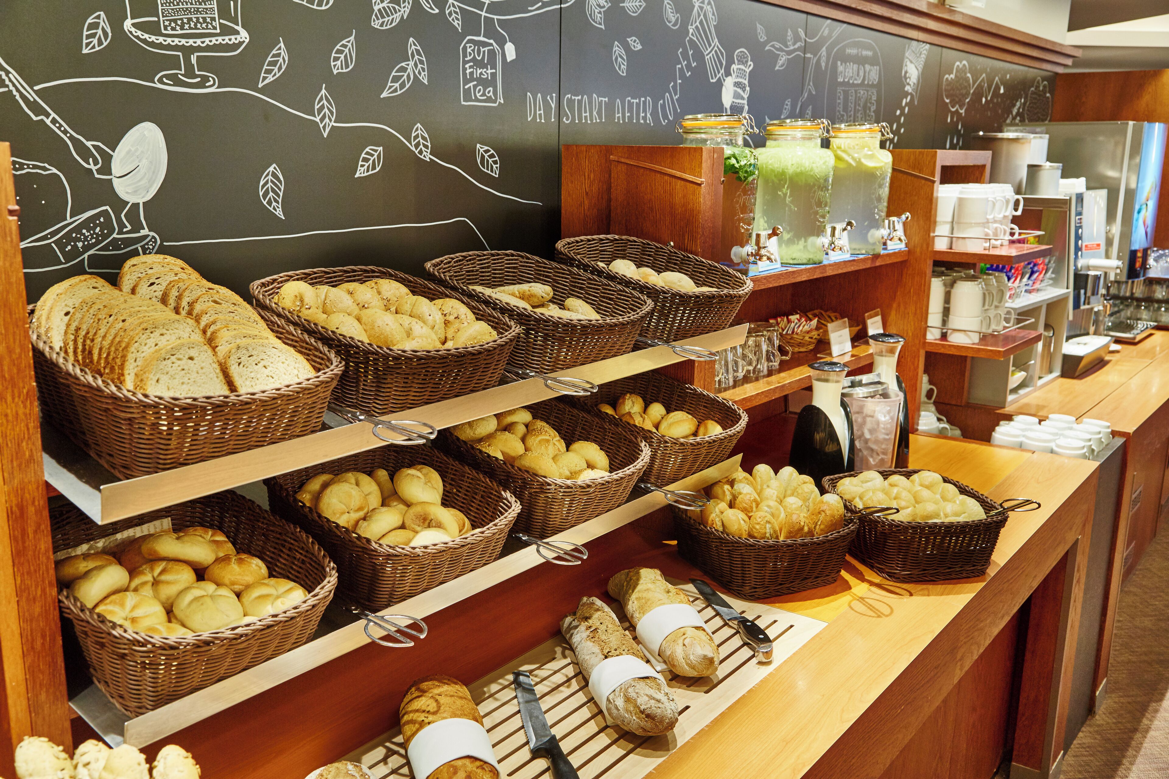 Buffet de café da manhã com diversos pães e doces dispostos em cestas.