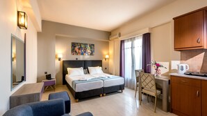 Quarto de hotel com cama, escrivaninha, cadeira e cozinha compacta.