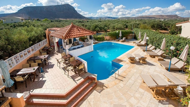 Uma área de piscina com espreguiçadeiras e um bar, rodeada por vegetação e uma montanha ao fundo.